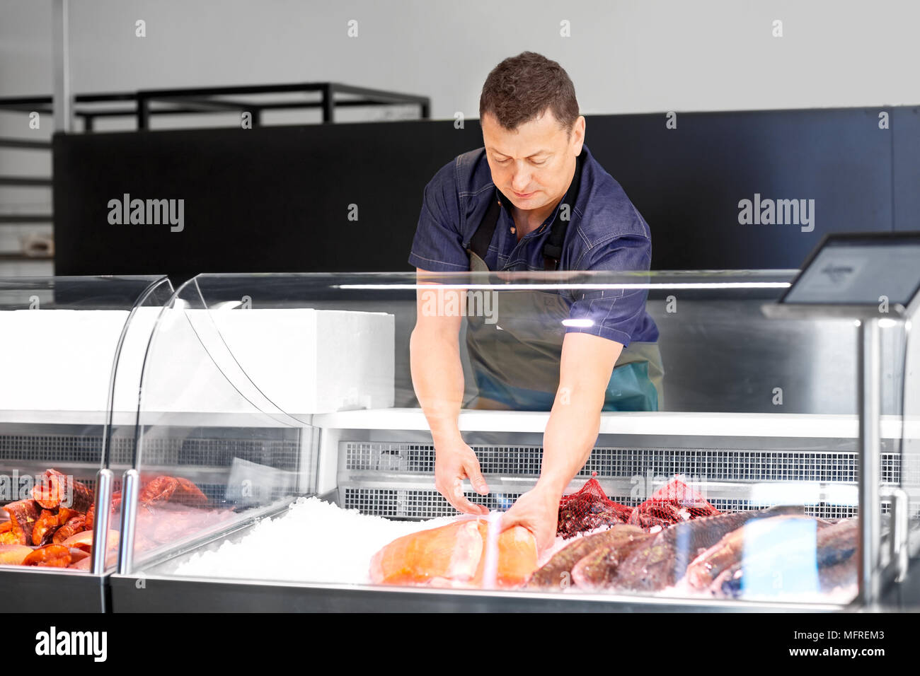 male seller with seafood at fish shop fridge Stock Photo - Alamy