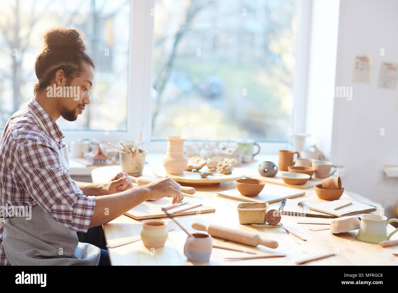 Side view of young mixed race male potter making beautiful clay ...