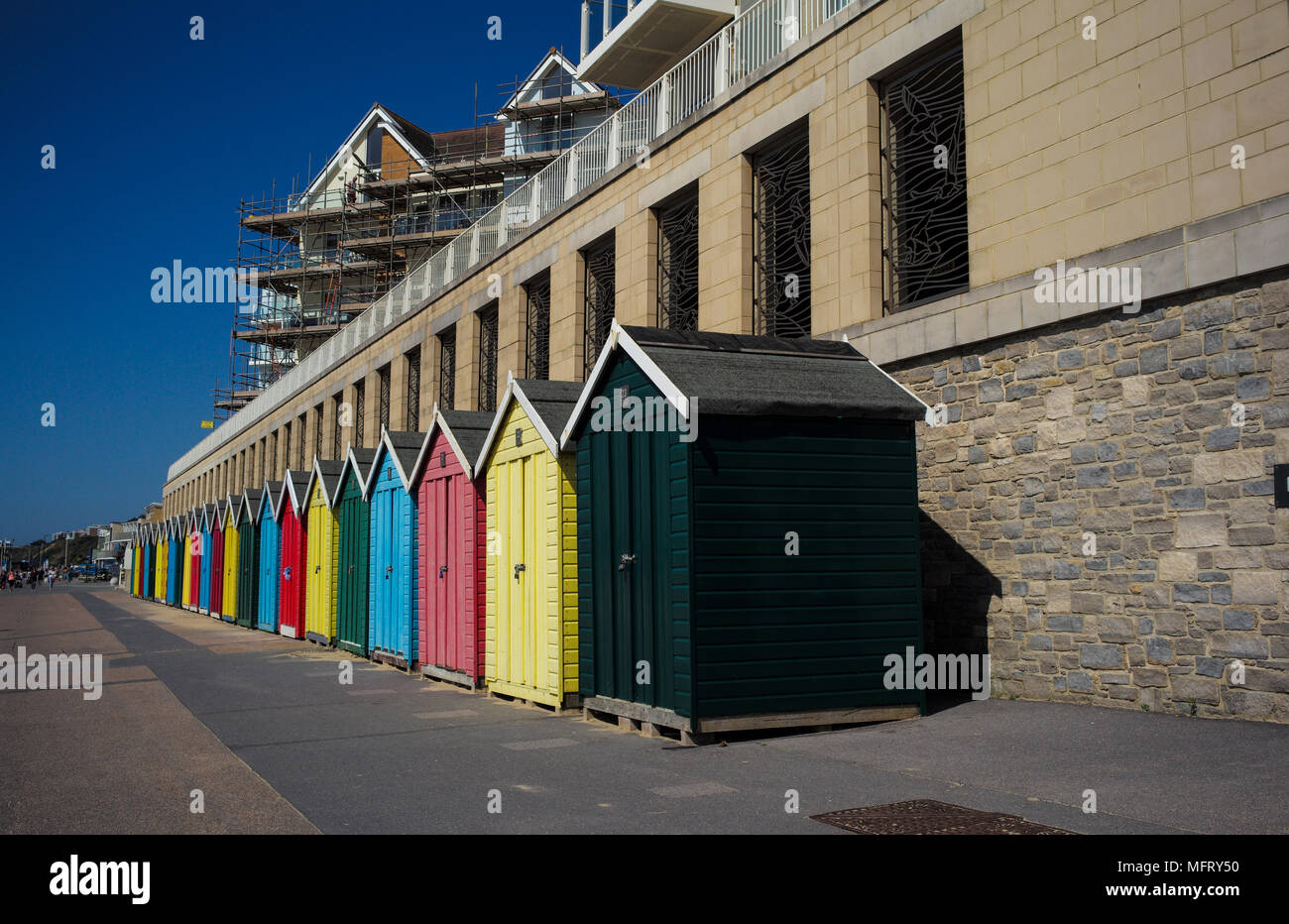 A line of multi coloured colourful locked and empty beach huts at ...