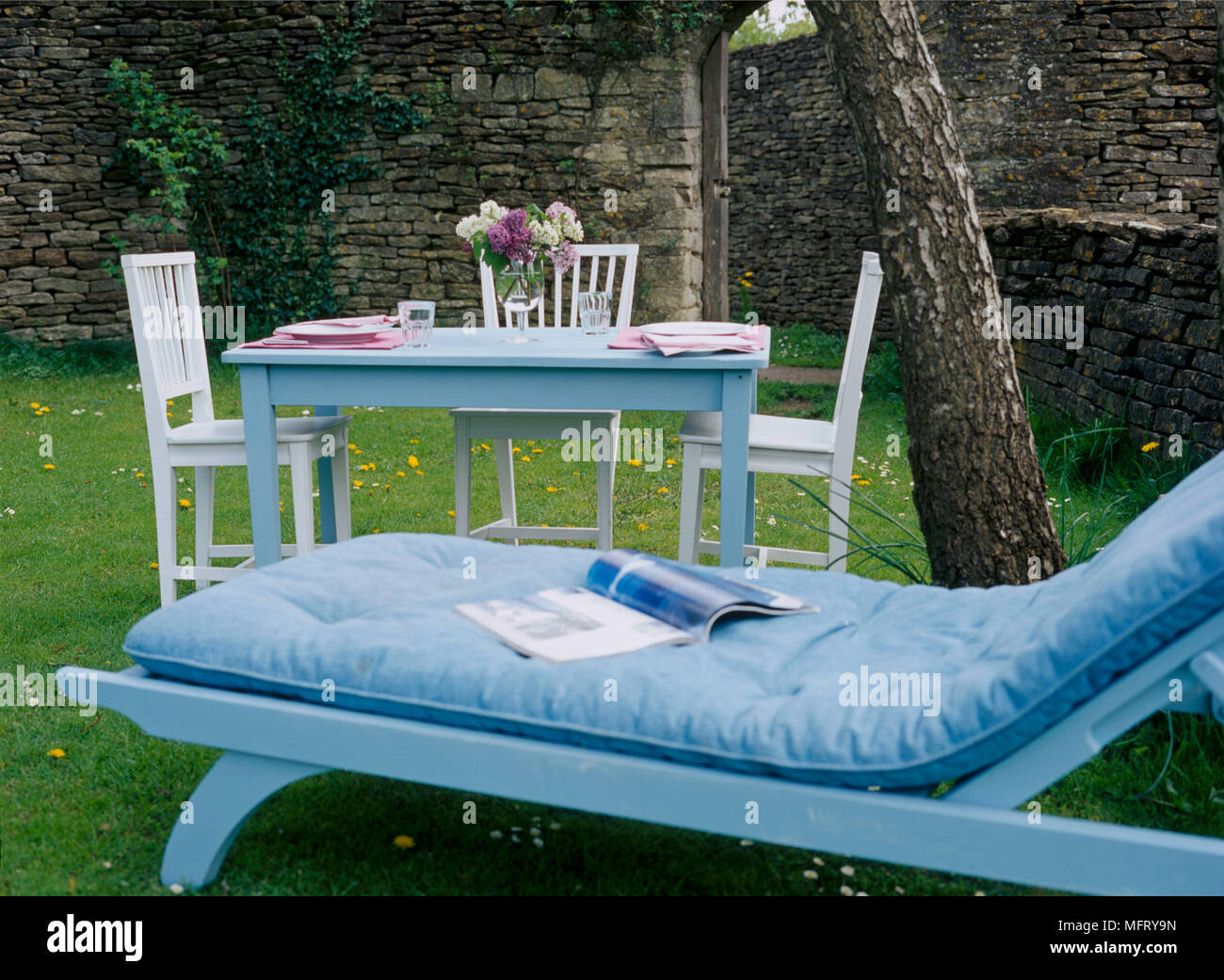 A detail of a walled garden with painted blue sun bed table and chairs ...