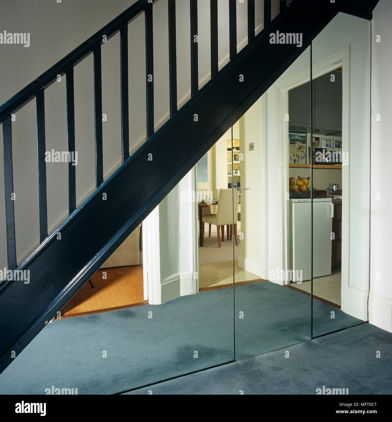 Mirrored wall beneath dark blue wooden staircase in modern hallway ...