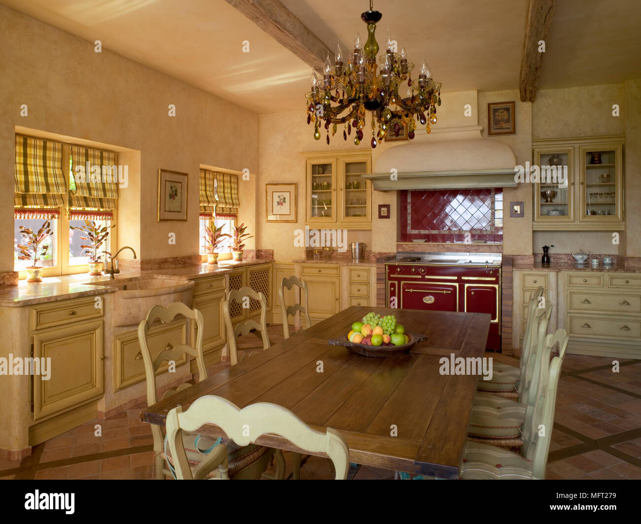 Kitchen with chandelier suspended above wooden dining table with chairs ...