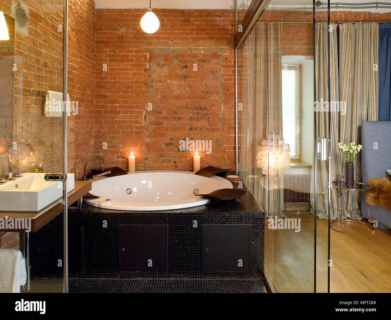 Bathroom with glass and exposed brick walls and large circular bath ...