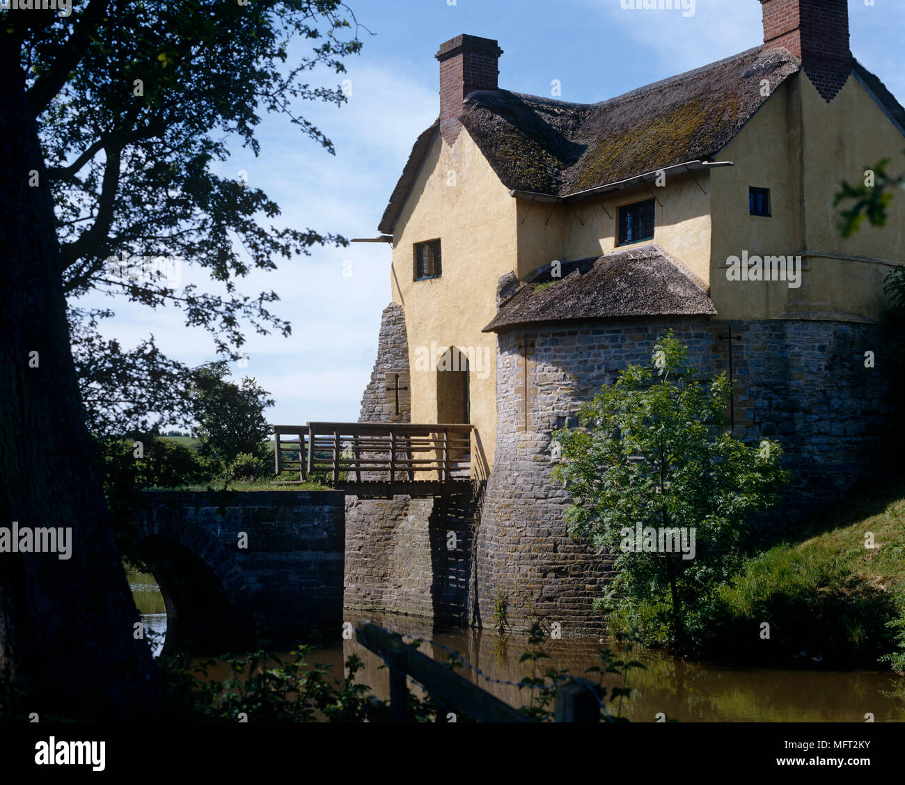 Exterior of stone country house with thatched roof and bridge to house ...