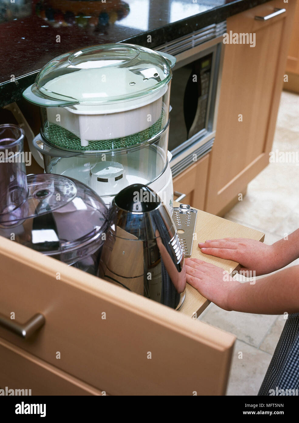 A detail of a modern kitchen, a woman pulling out drawer of wooden unit ...