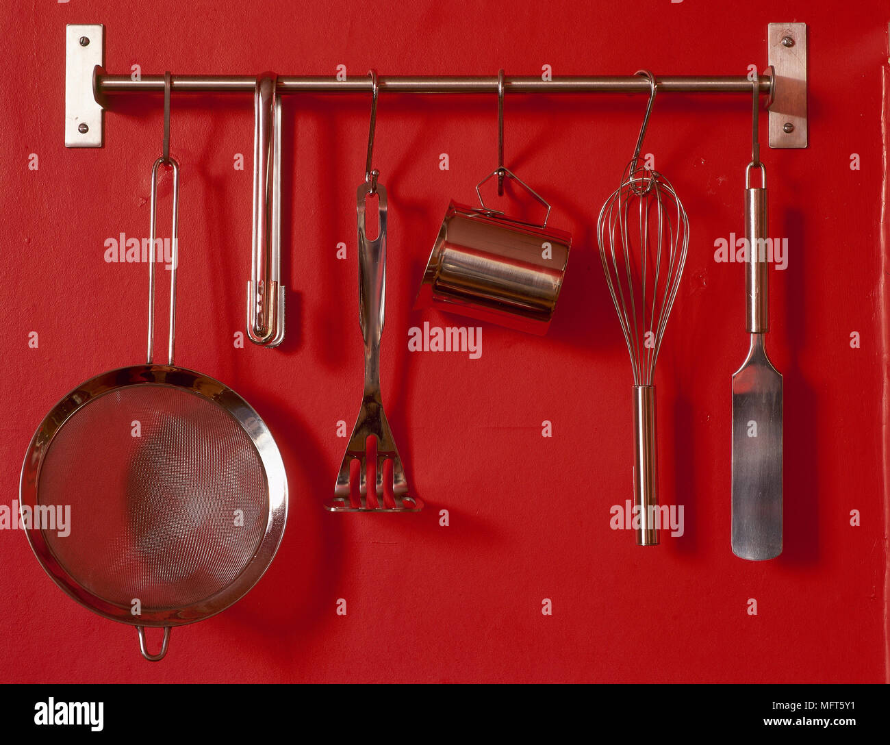 A detail of a red kitchen, stainless steel utensils, hanging from rod ...