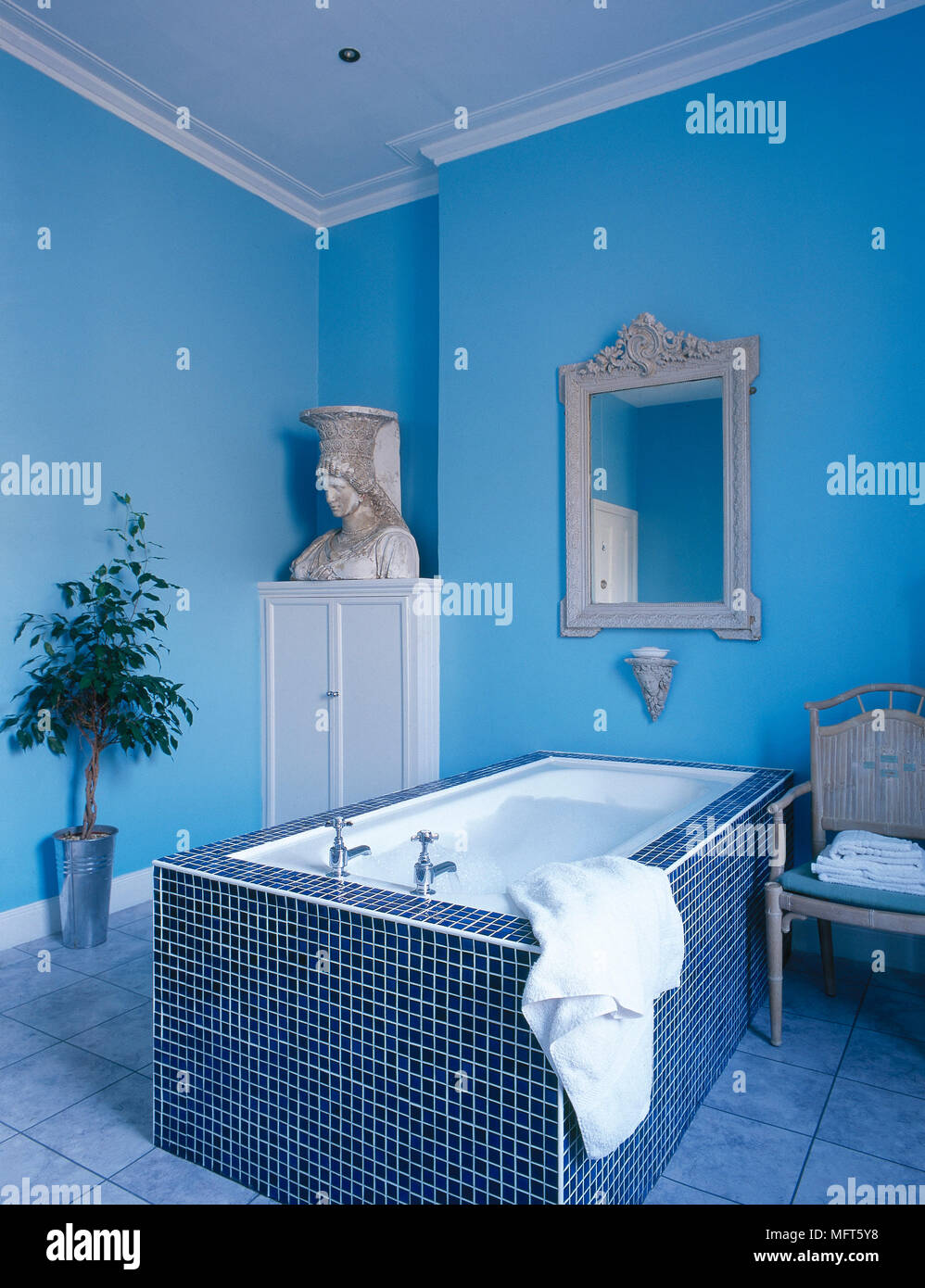 A modern bathroom with blue walls, bath with mosaic tiled surround ...