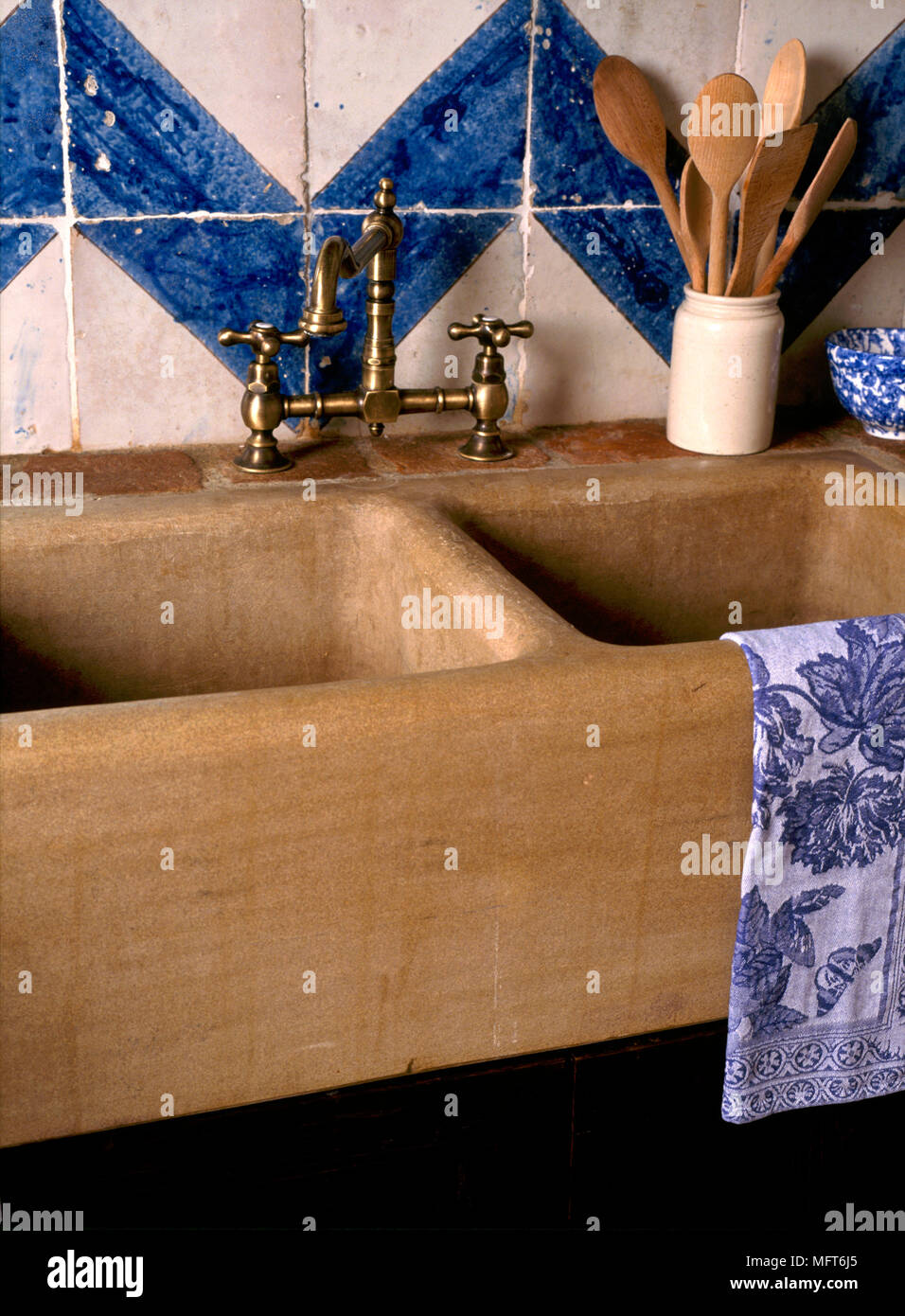 A detail of a rustic country kitchen showing a double sink, brass taps ...