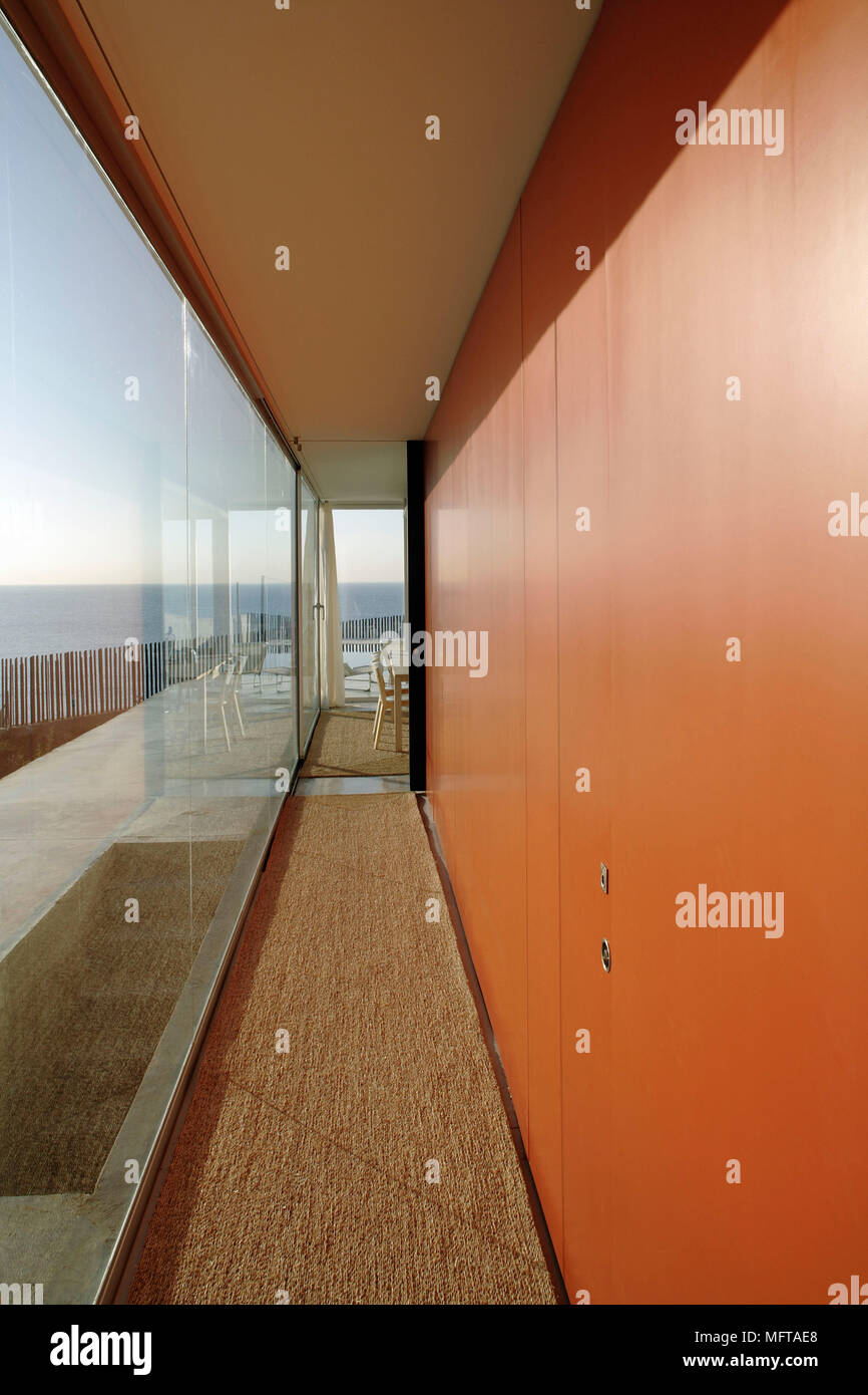 View along narrow orange corridor enclosed by floor to ceiling windows ...