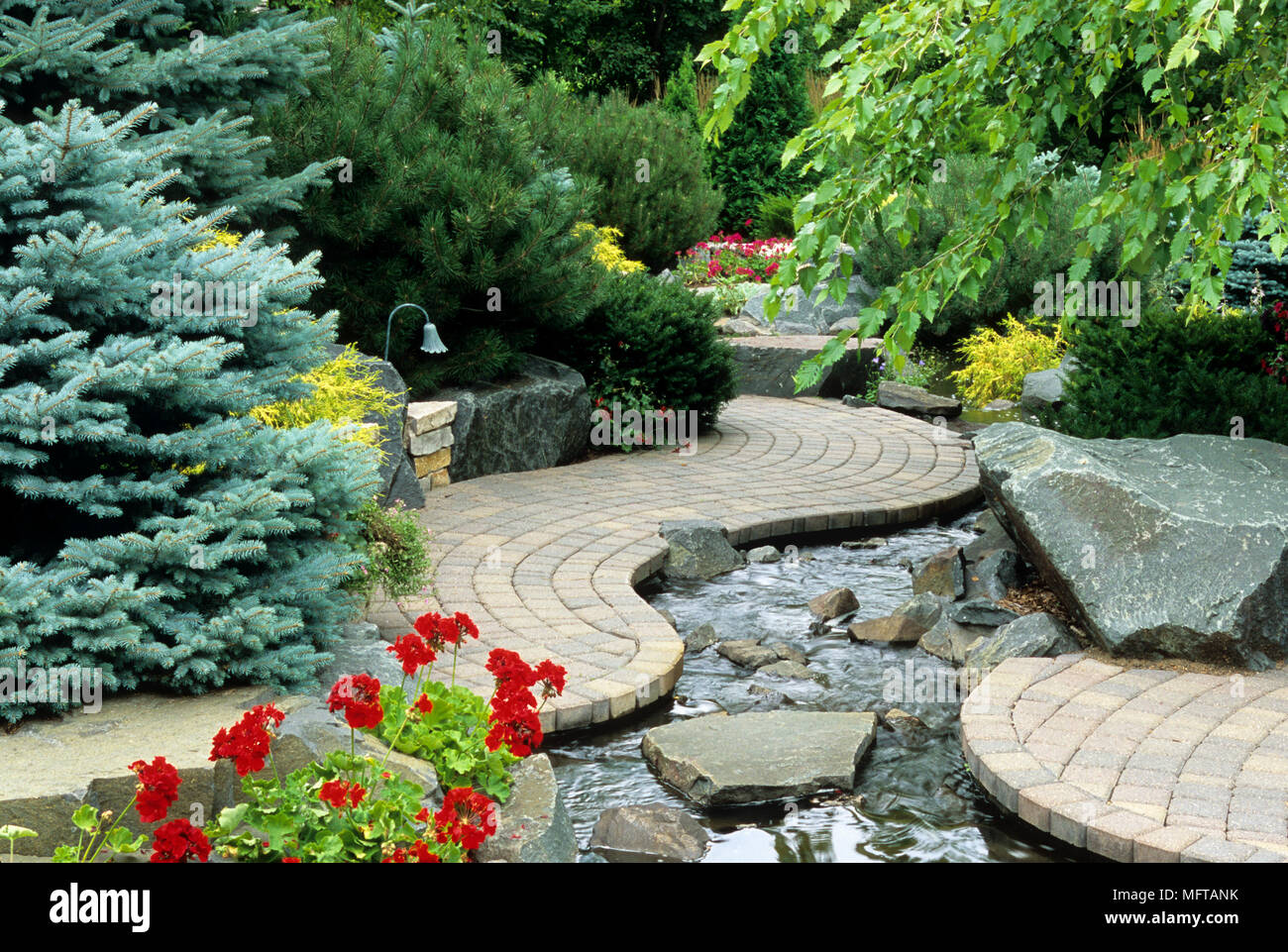 Garden with stream in between brick path and boulders Stock Photo - Alamy