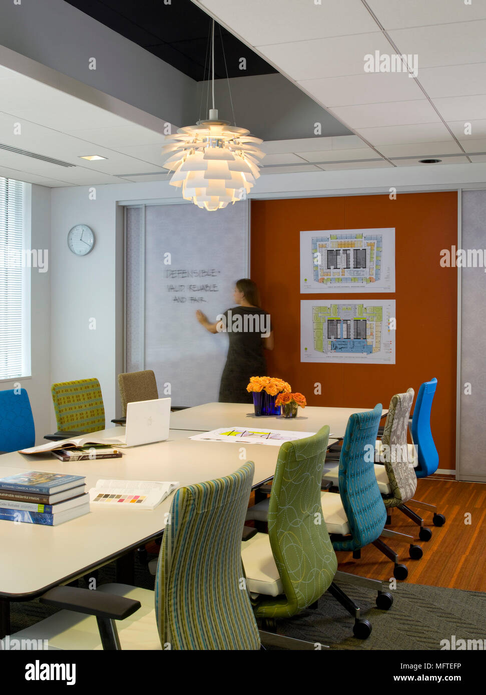 Table and chairs in office conference room with woman writing on board ...