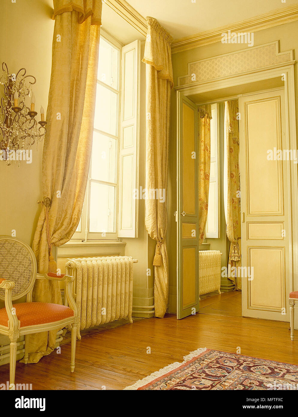Upholstered chair next to window with gold curtains Stock Photo - Alamy