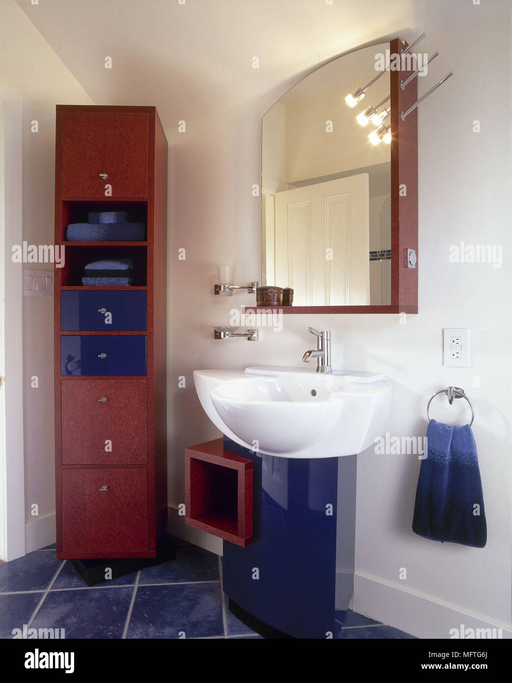Modern bathroom with wash basin under lit mirror and tall storage unit ...