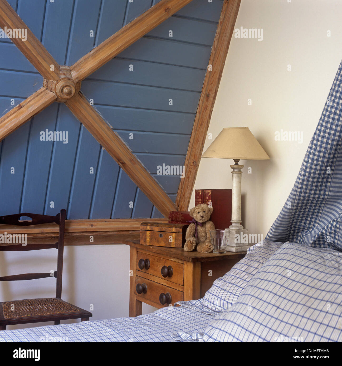 Lamp on bedside table next to double bed with blue check pattern cover ...