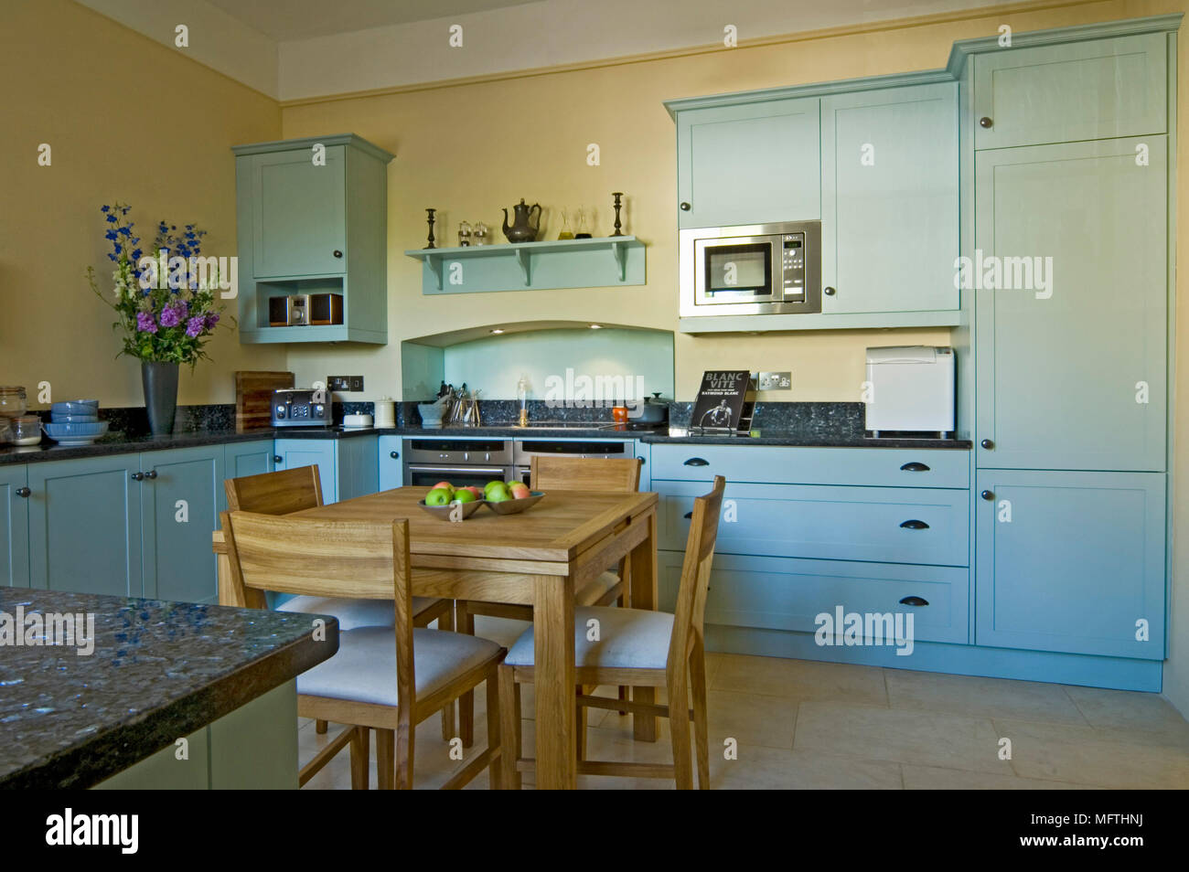 Wooden table and chairs in centre of kitchen with blue units Stock ...