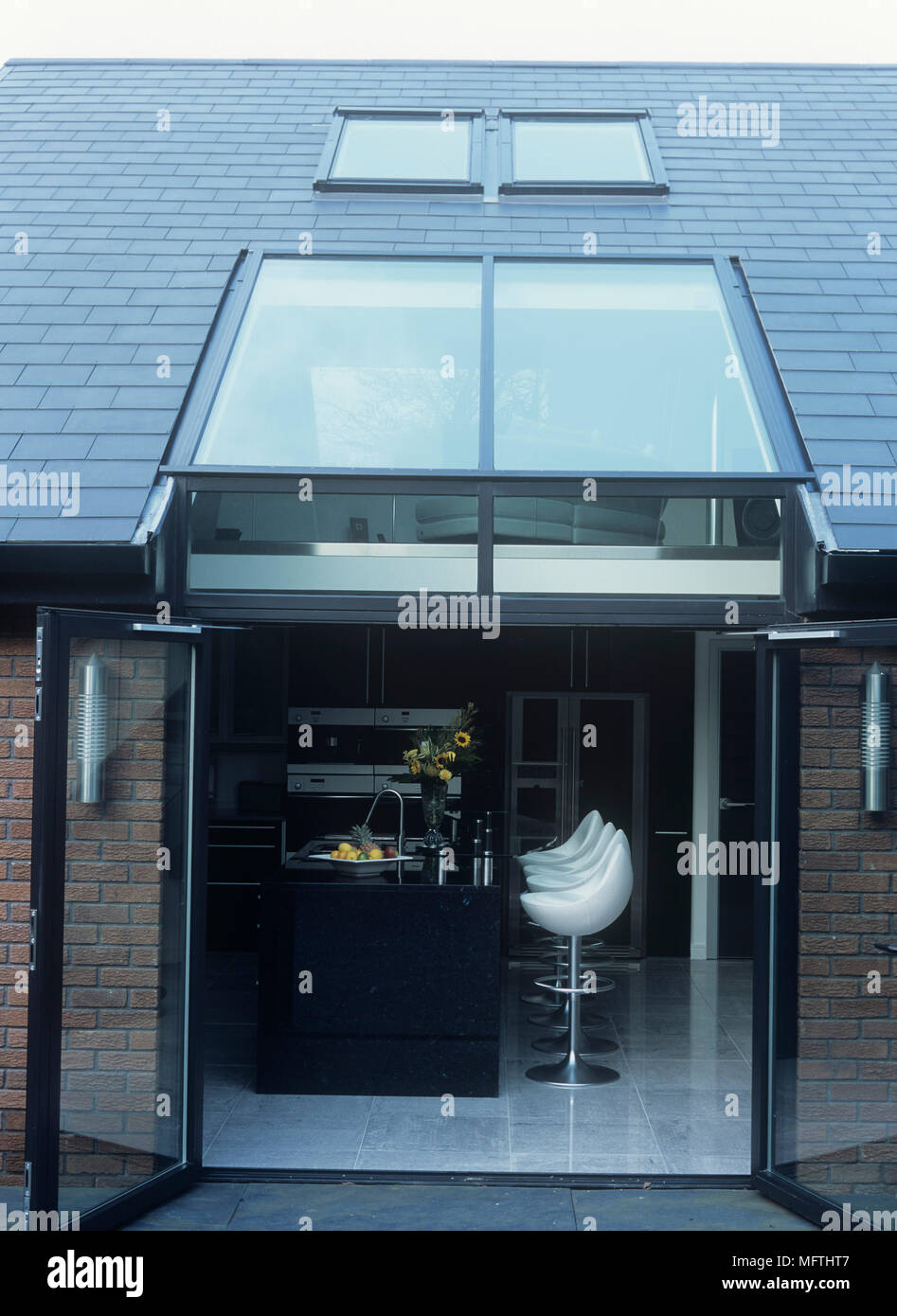 An exterior view of open glass doors leading into a modern kitchen ...