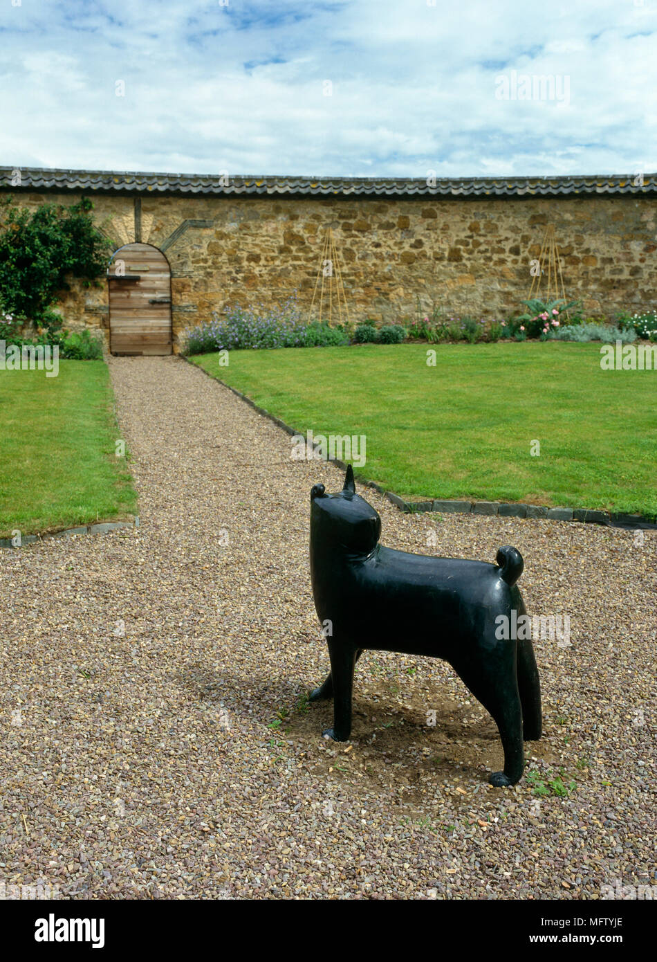 Dog sculpture on gravel path bordered by lawn in walled garden Stock ...