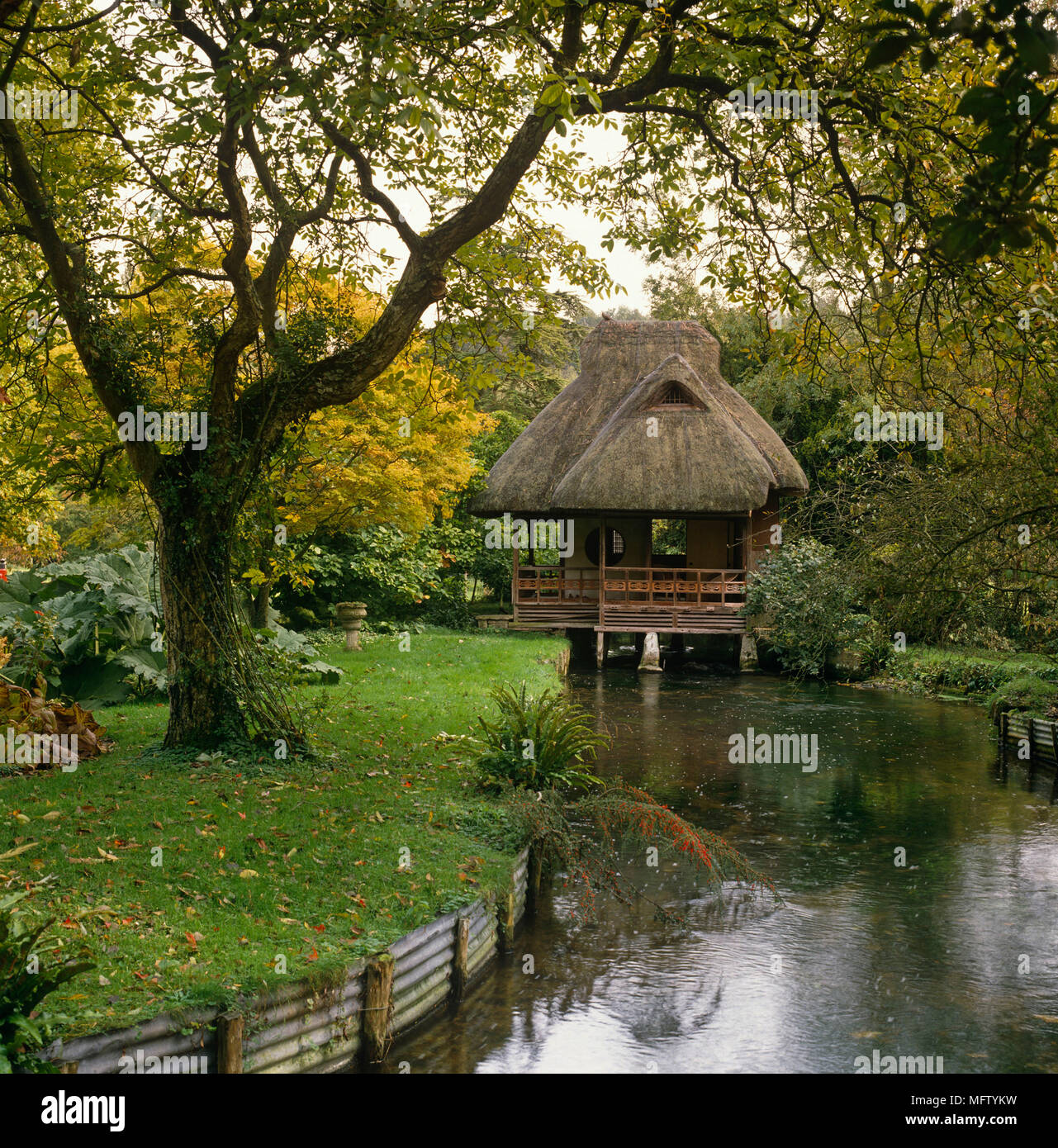Thatched summer house set amongst trees next to pond in garden Stock ...