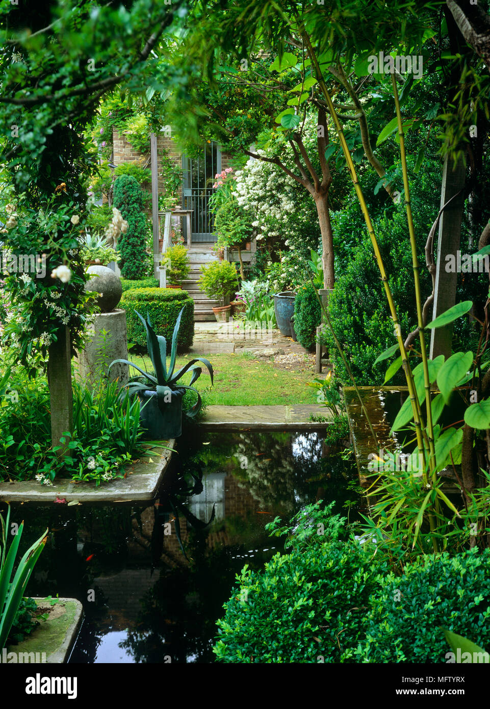 View across garden pond to lawned area beyond set amongst trees and ...