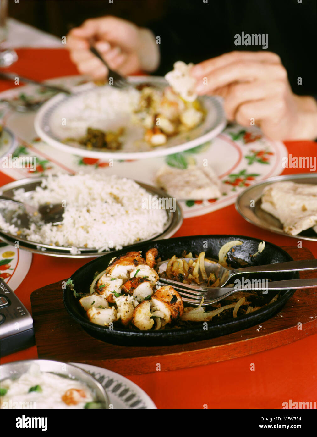 Person eating in Indian restaurant at table laid with chicken tikka ...