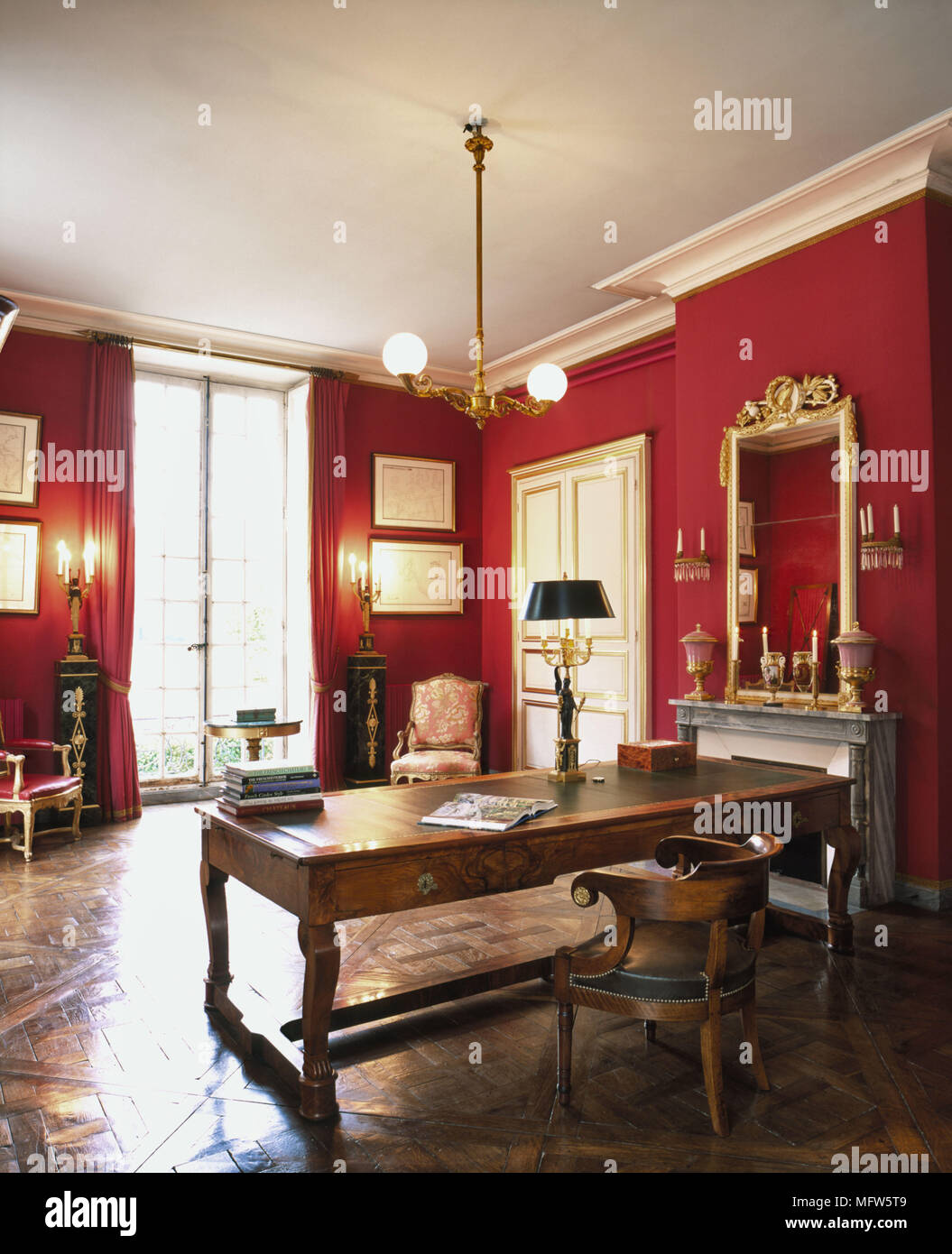 A traditional red study room fireplace gilt mirror globe light lit ...
