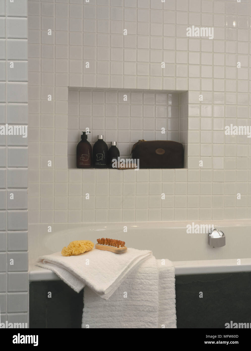 Details of a bath surrounded white tiles and inbuilt ledge full of ...