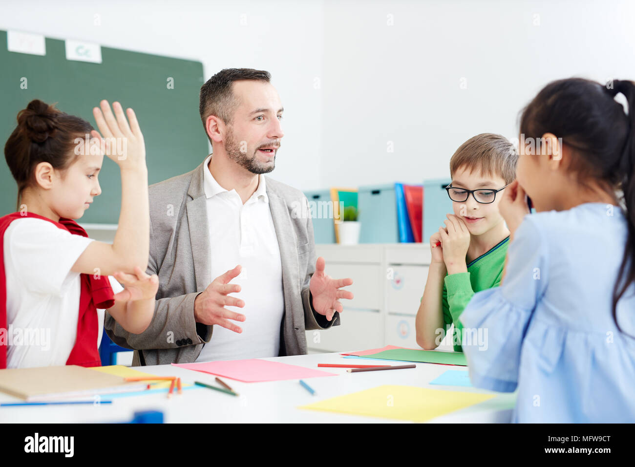 Group of Caucasian 1st graders sitting at desk with professional male ...