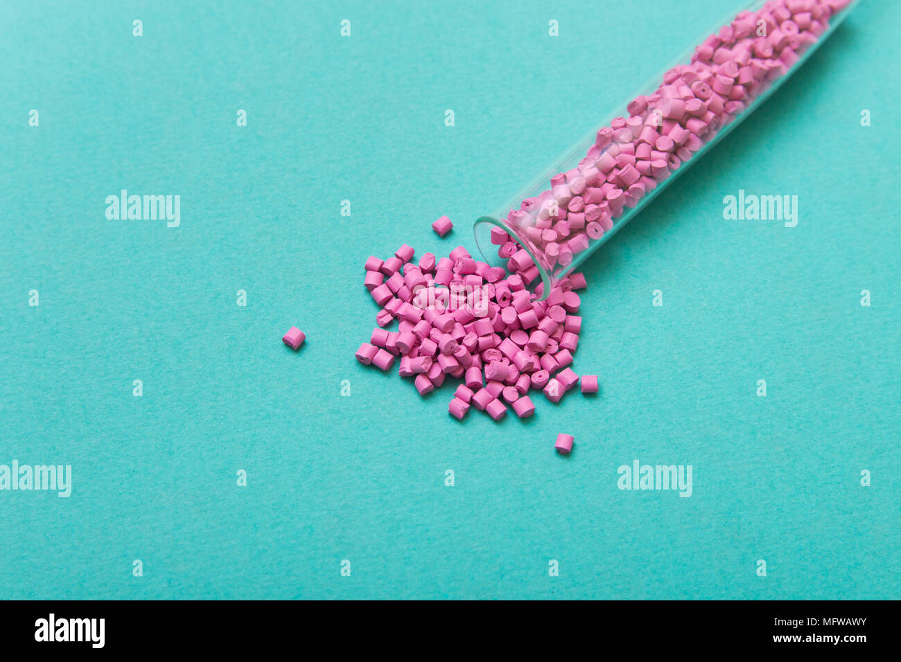 Plastic pellets. Pink Plastic granules from the tube on a turquoise ...