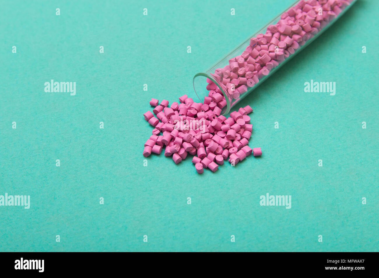 Plastic pellets. Pink Plastic granules from the tube on a turquoise ...