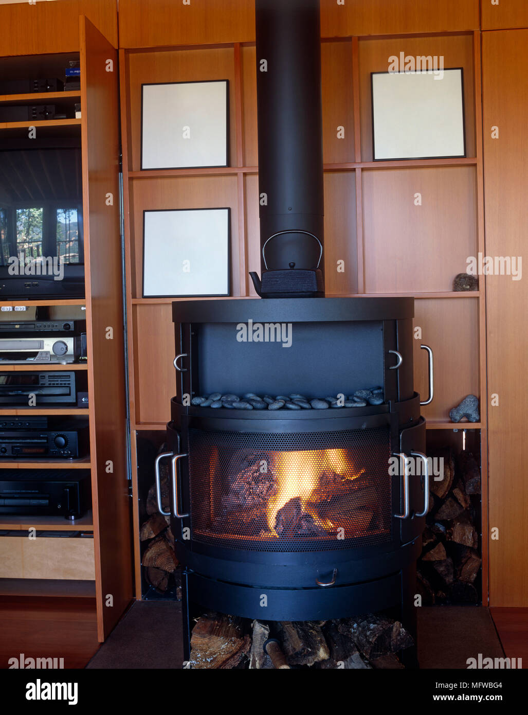 Stove with lit fire and chimney in front of built in cupboard and ...