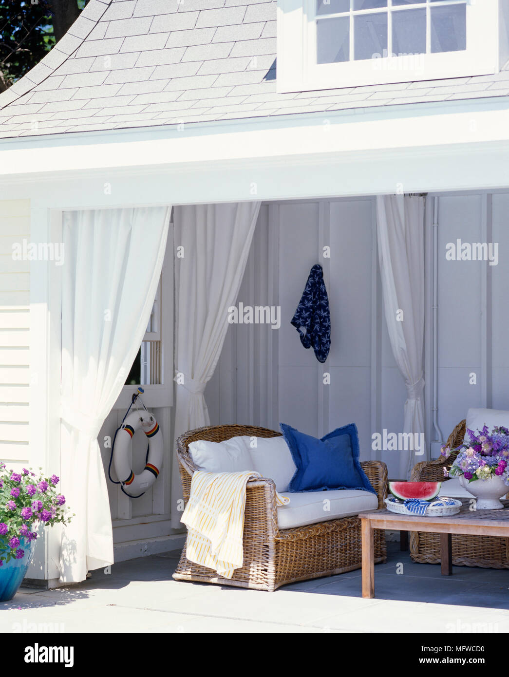 Cane sofa on covered terrace with white curtains Stock Photo - Alamy