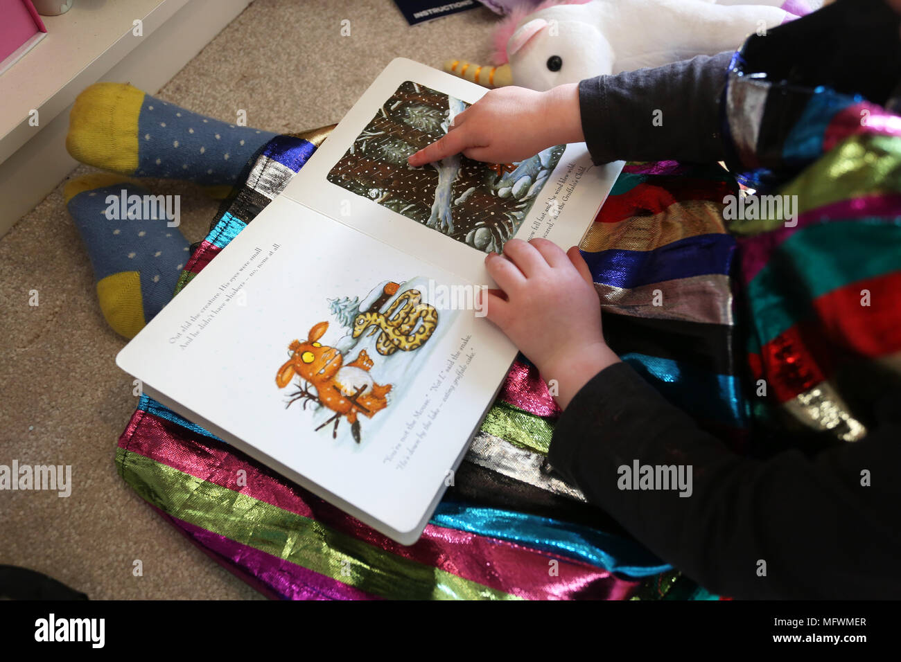 A young girl reading books in her bedroom dressed in cool colourful ...