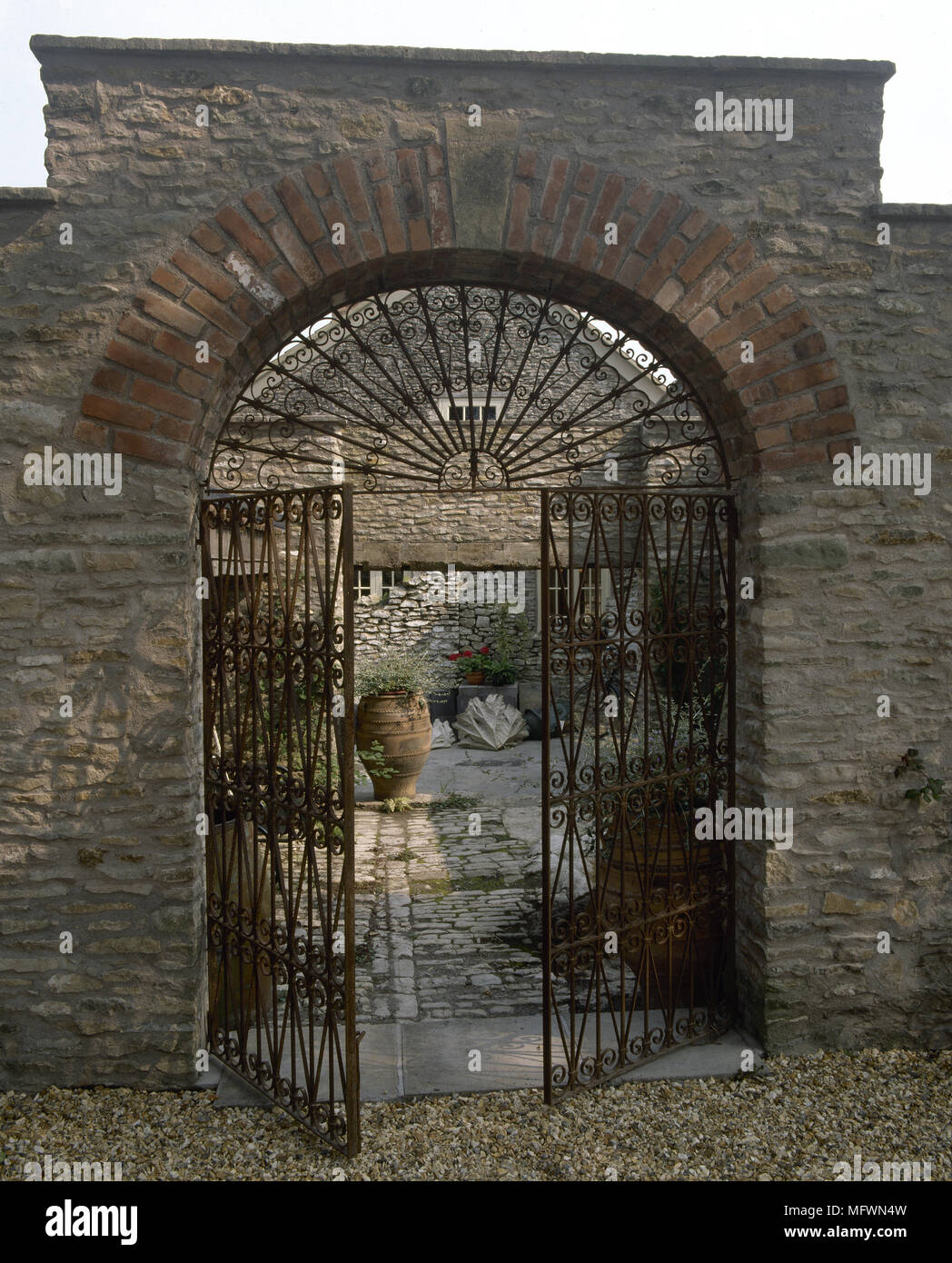 Stone wall with arch and wrought iron gates Stock Photo - Alamy