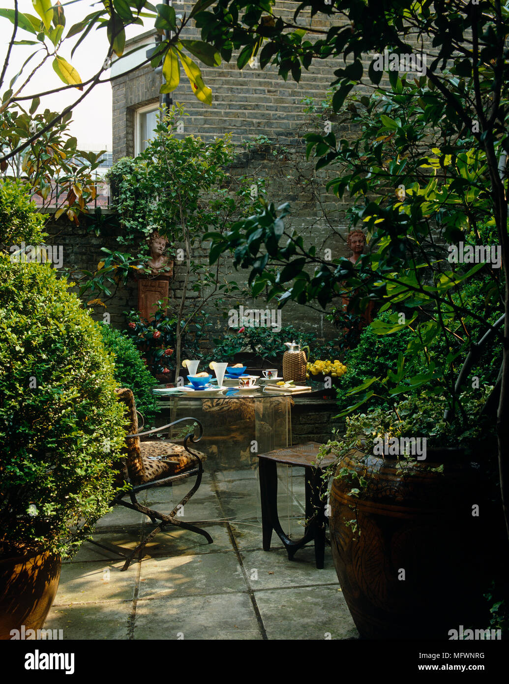 Table and chairs set on secluded paved patio area Stock Photo - Alamy