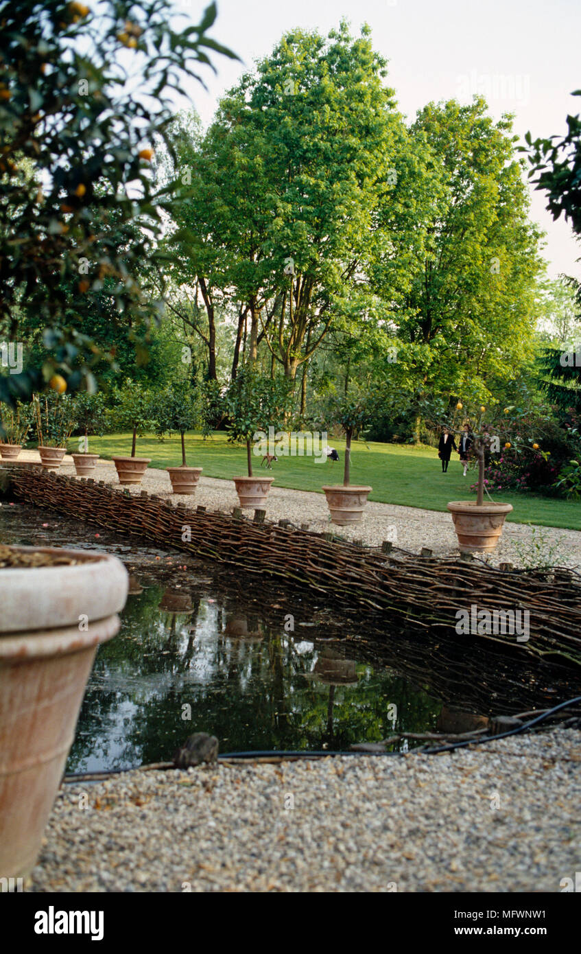 Pond with woven wooden border lined with pot plants Stock Photo - Alamy