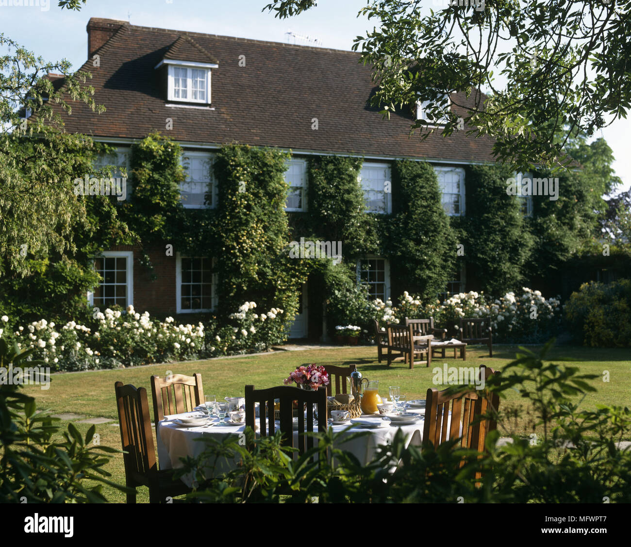 Table with place settings in garden of country house covered in foliage ...