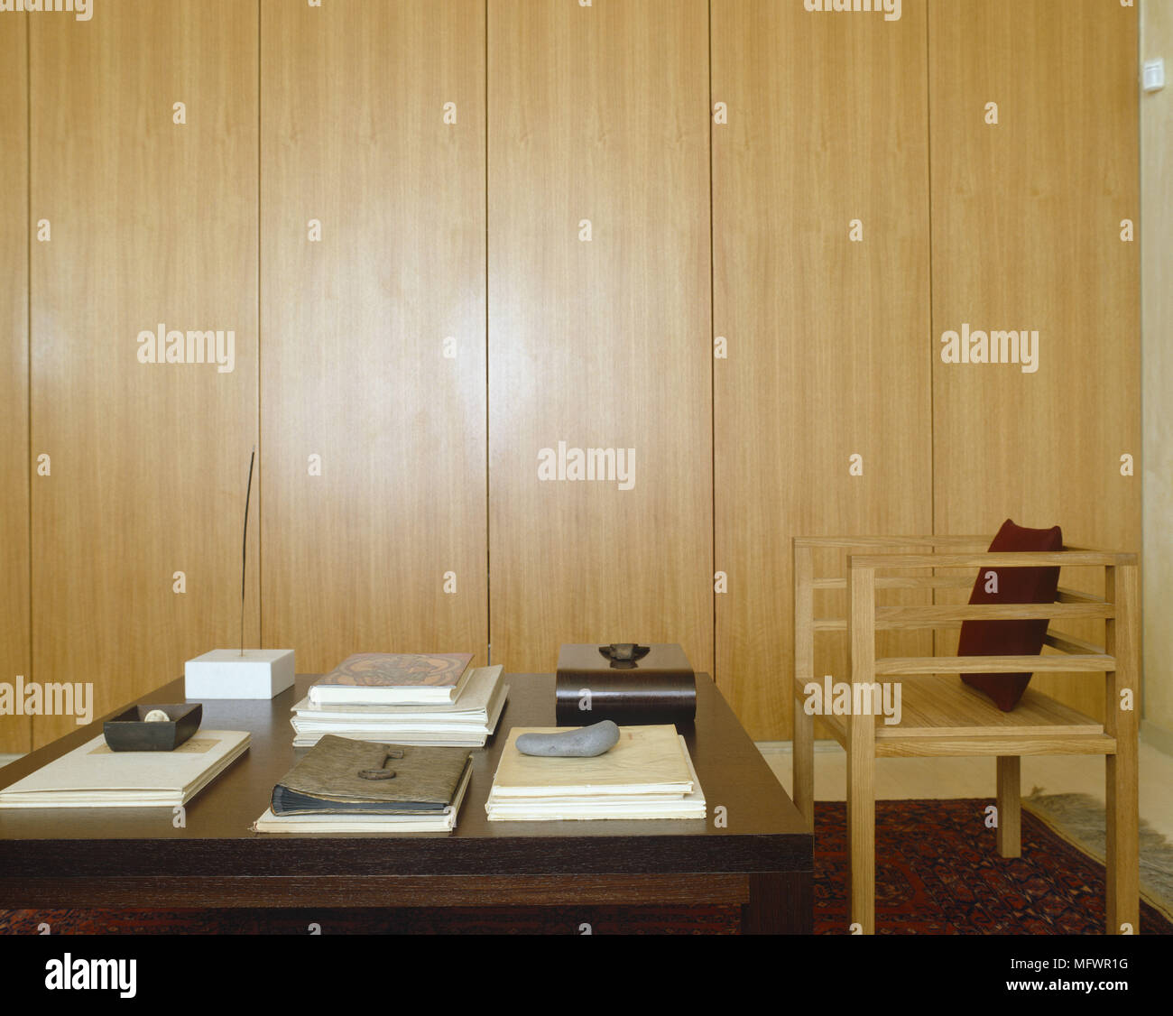 Wooden chair facing table with books in front of wood panelled wall ...