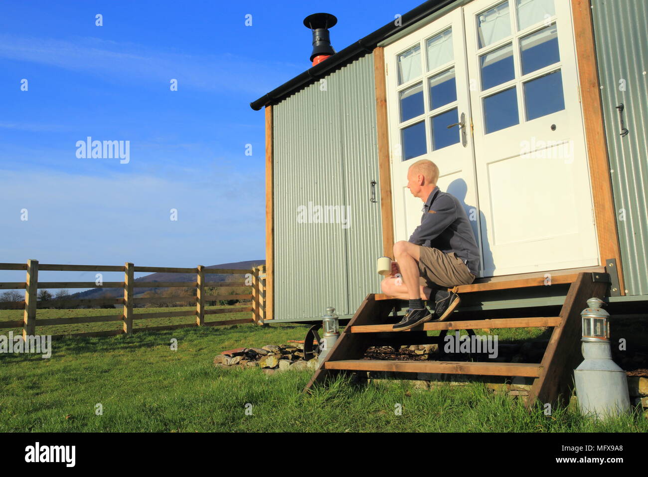 sitting on steps of a sheperds hut drinking coffee with a blue sky ...
