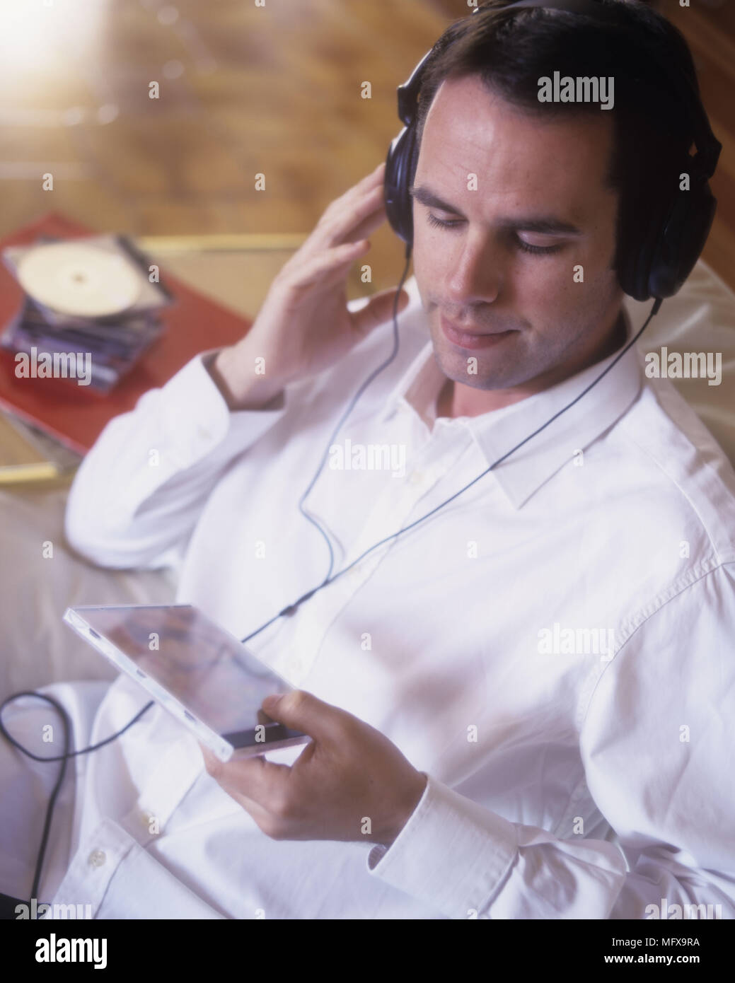 Man wearing white shirt looking at CD case and listening to music ...