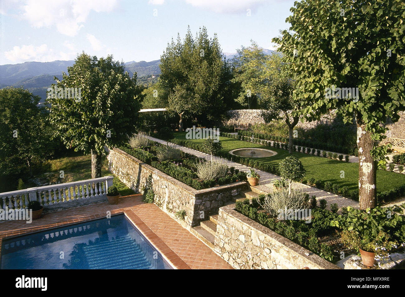 Outdoor swimming pool surrounded by garden with trees and walled flower ...