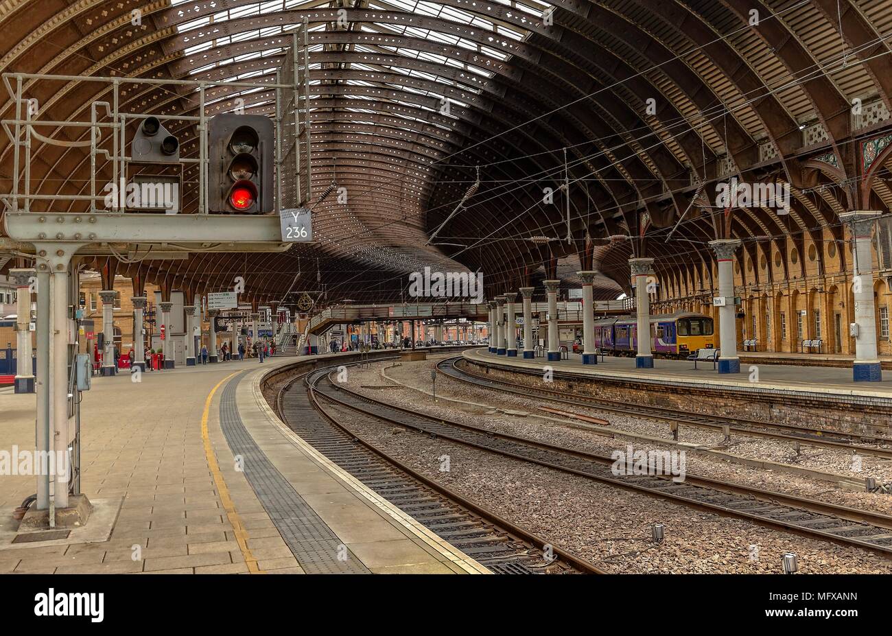Train signal light on red over a station platform. A train waits in a ...