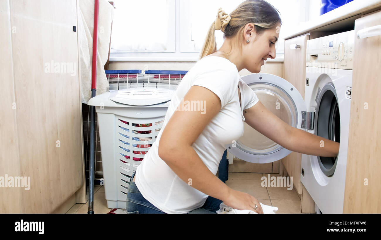 Portrait of beautiful blonde woman loading clothes in washing machine ...