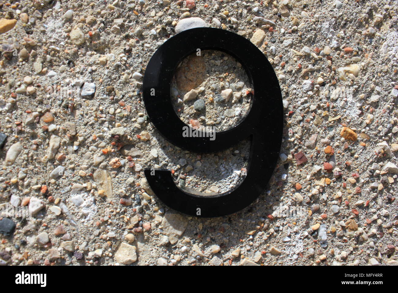 The number nine as a black plastic text glued to a textured pebble ...