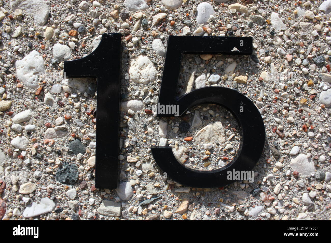 The number fifteen as a black plastic text glued to a textured pebble ...