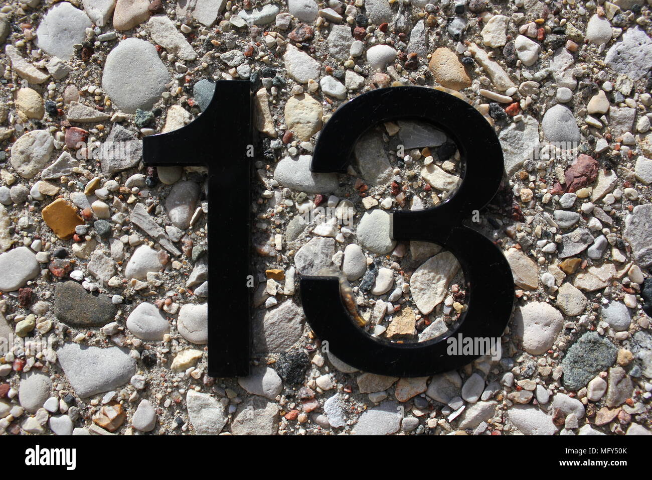 The number thirteen as a black plastic text glued to a textured pebble ...