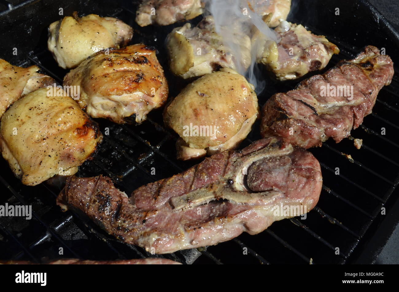 Pork Steaks and Chicken Thighs cooking on the outside BBQ grill on a ...