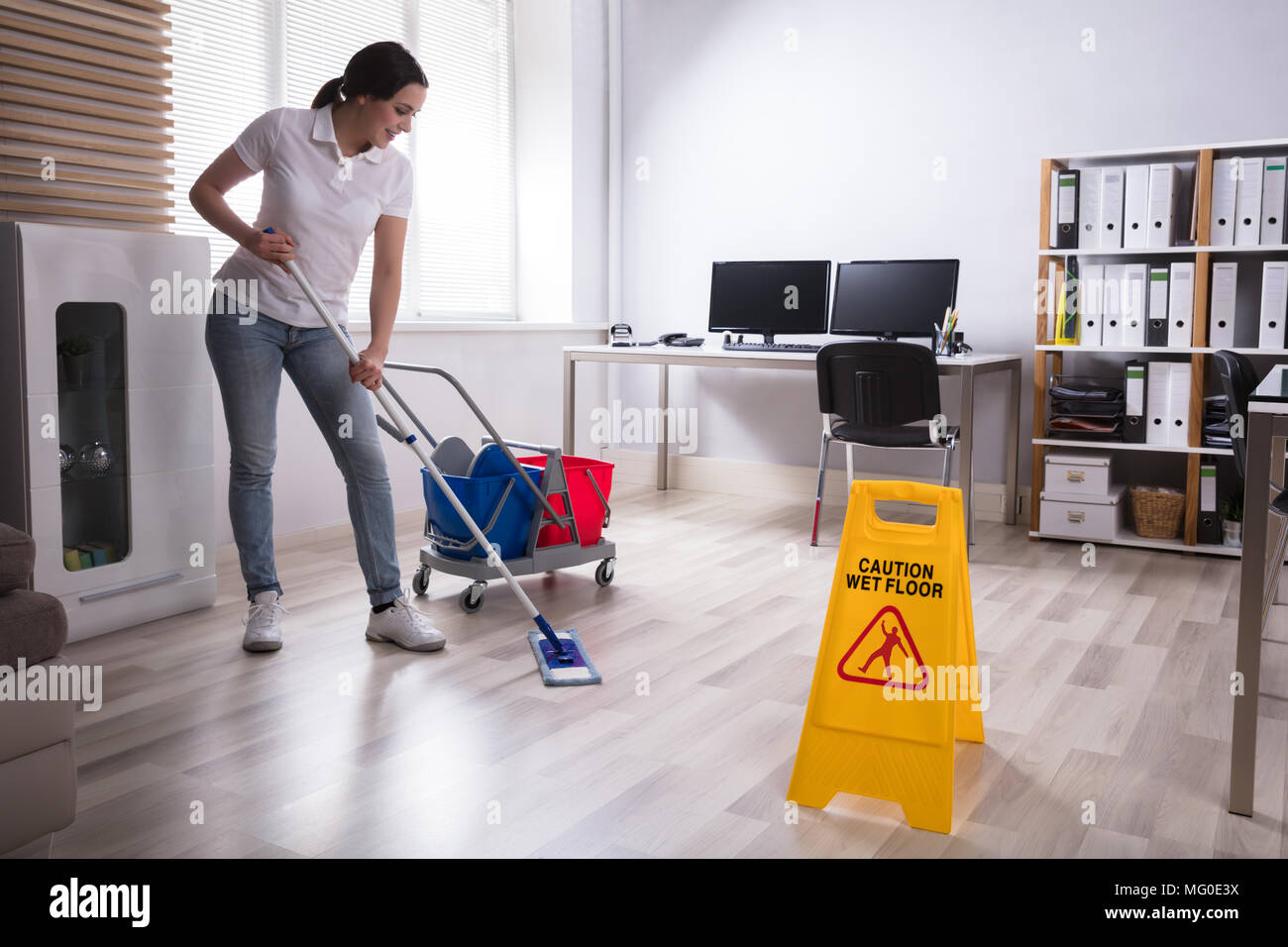 Female Janitor Cleaning Office With Wet Floor Caution Sign On Floor ...