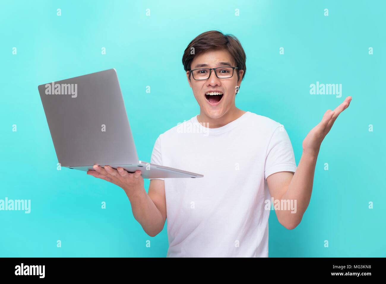 A happy excited young asian man with a laptop and showing a fist of ...