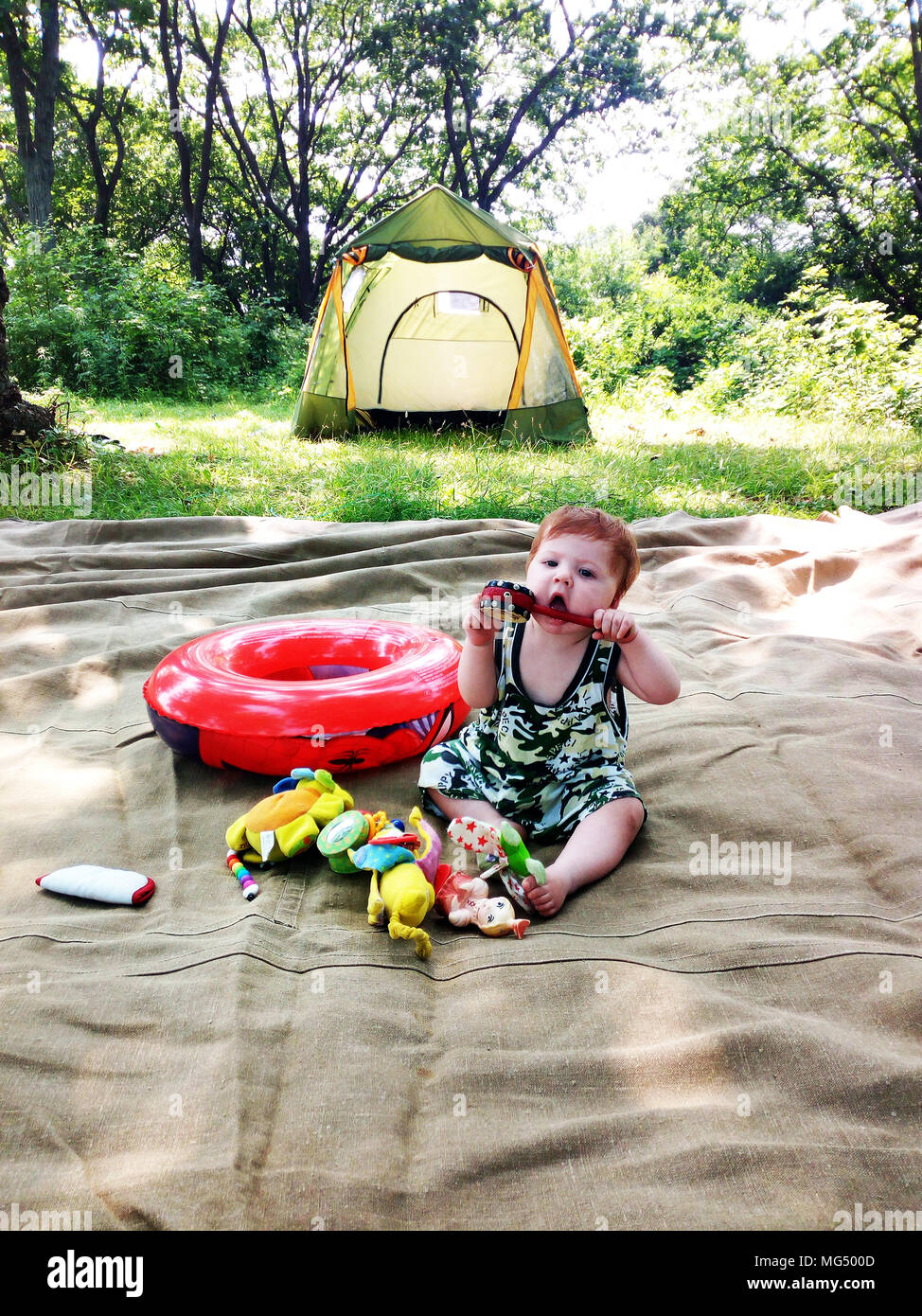 Cute ginger little baby boy with toys around sitting at camping place ...