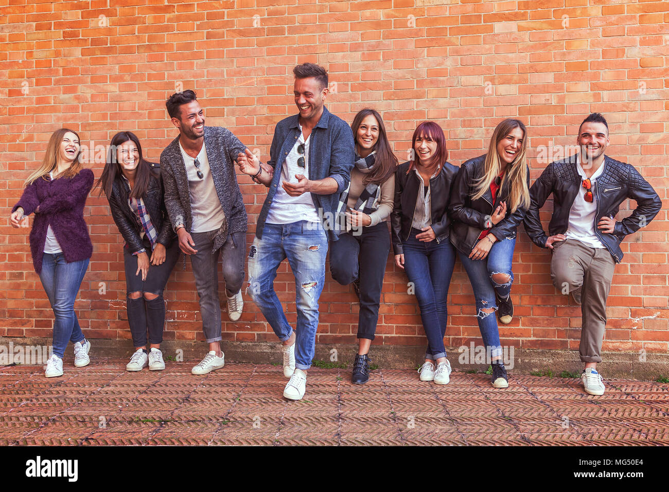 large group of friends meeting to have fun in front of a brick wall ...